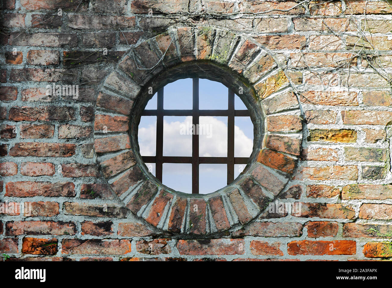 Circular windows with a metal grate against an old brick wall with sky ...