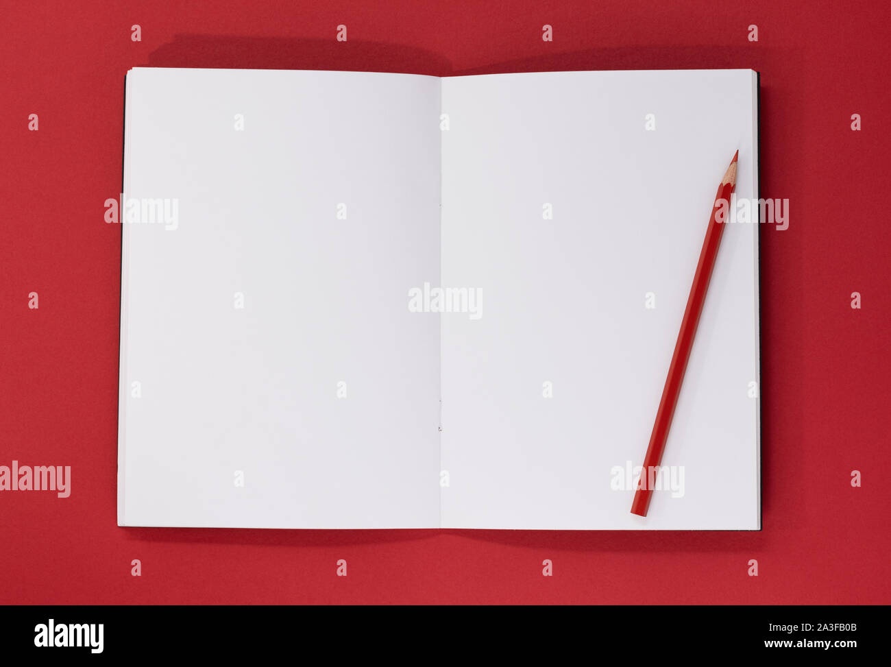Open blank notepad and red pencil on a red background, with copy space ...