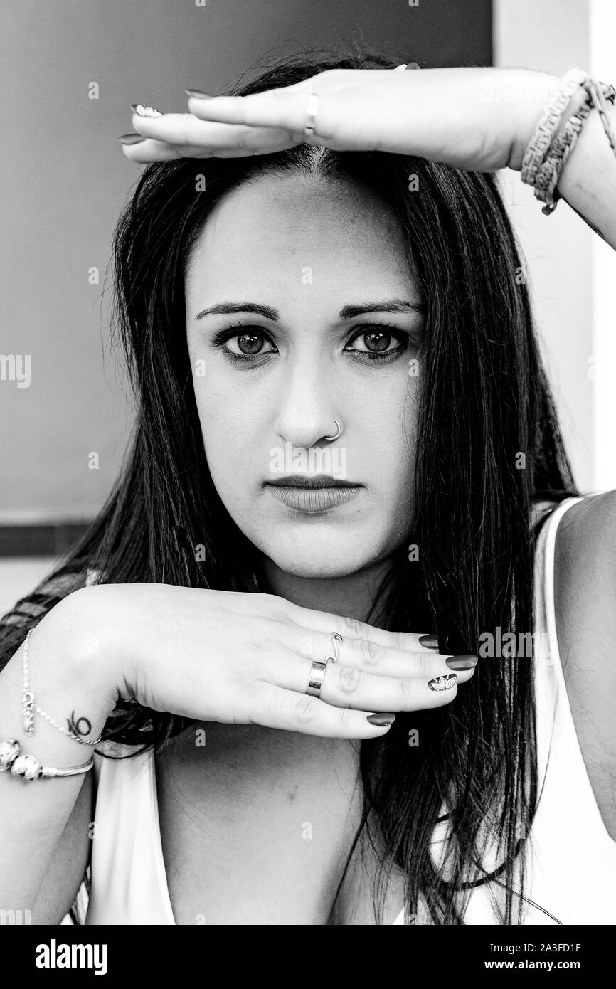 Portrait of a young woman framing her face with hands in serious pose ...