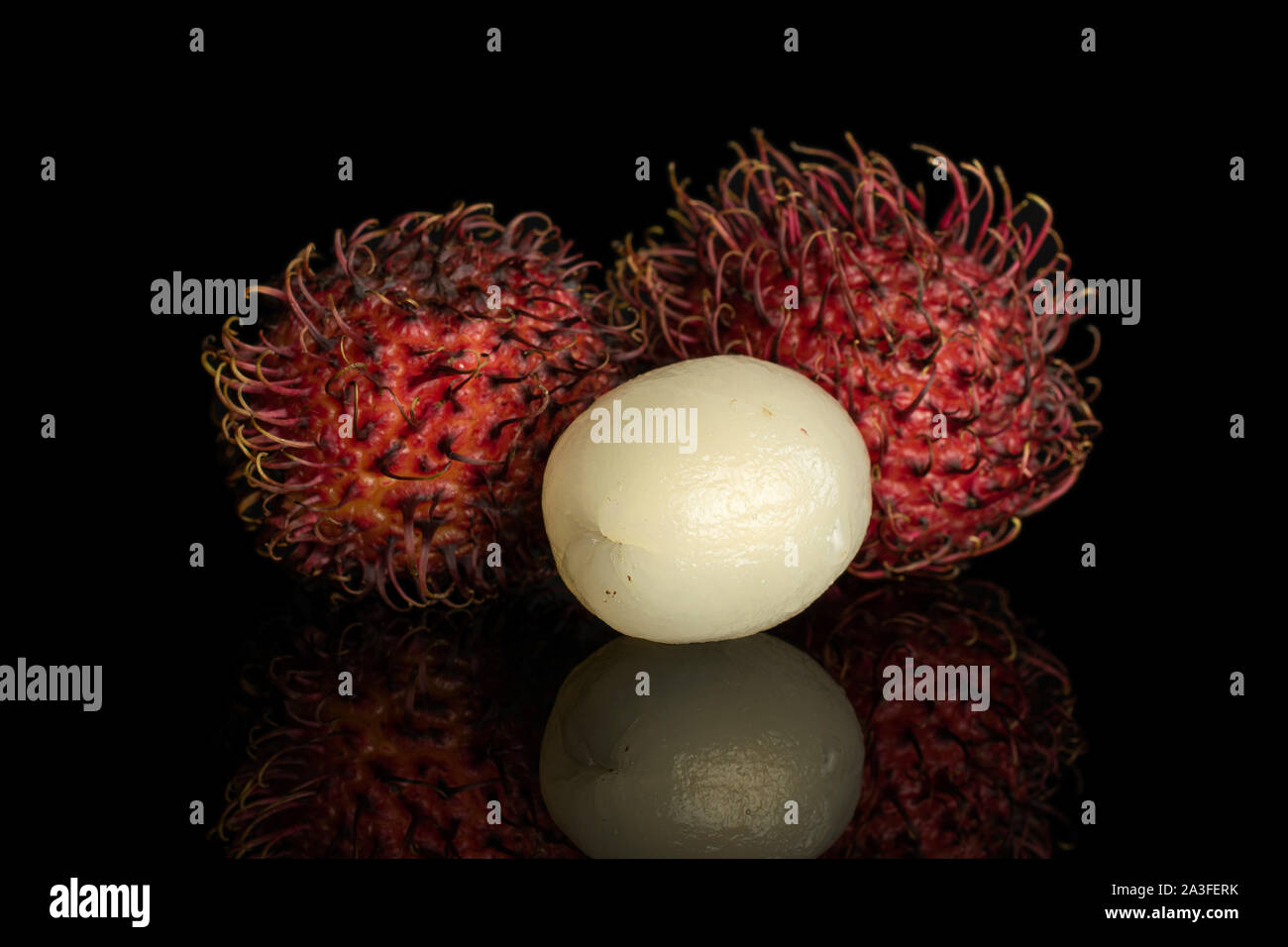 Group of three whole fresh red rambutan one peeled isolated on black ...