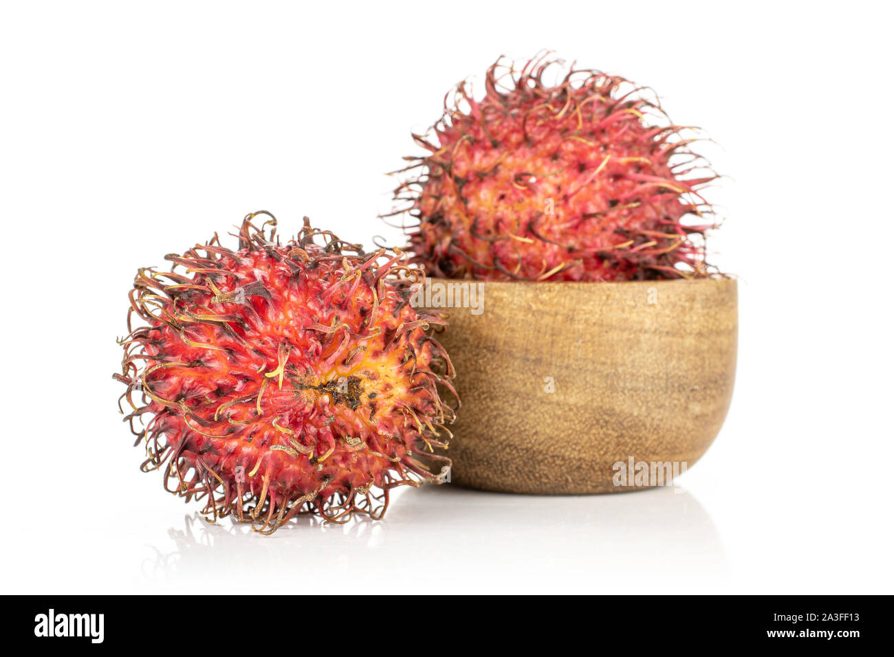 Group of two whole unpeeled fresh red rambutan in wooden bowl isolated ...