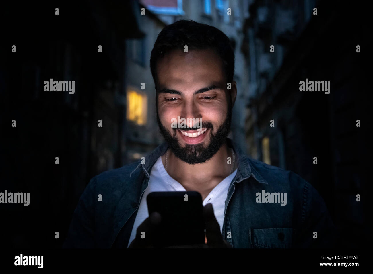Bearded smiling man holding smartphone with light reflection on the ...