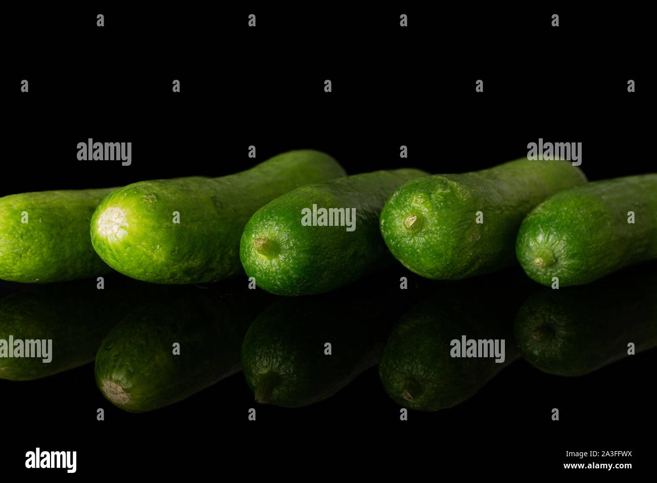 Group of five whole mini green cucumber isolated on black glass Stock ...