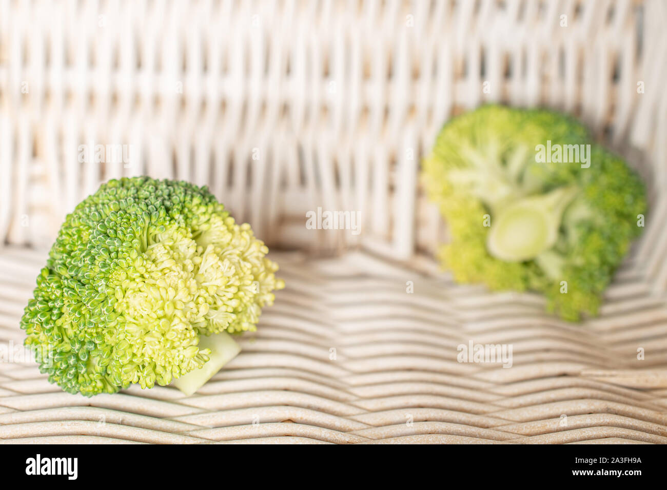 Group of two whole fresh green broccoli with braided rattan behind ...