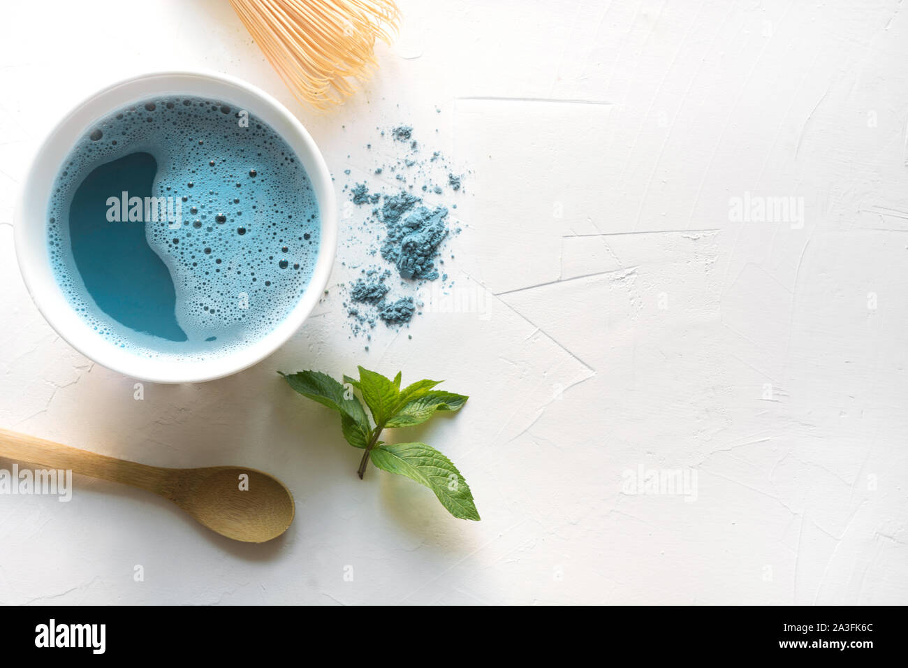 Ceremony blue matcha tea in bowl and bamboo chasen on white concrete ...