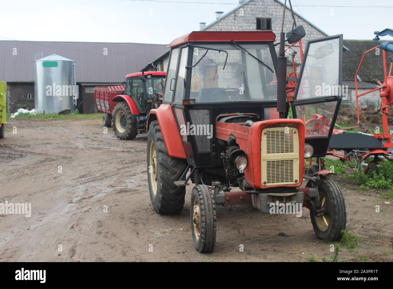 Red tractors and agricultural equipment in the courtyard of a dairy ...