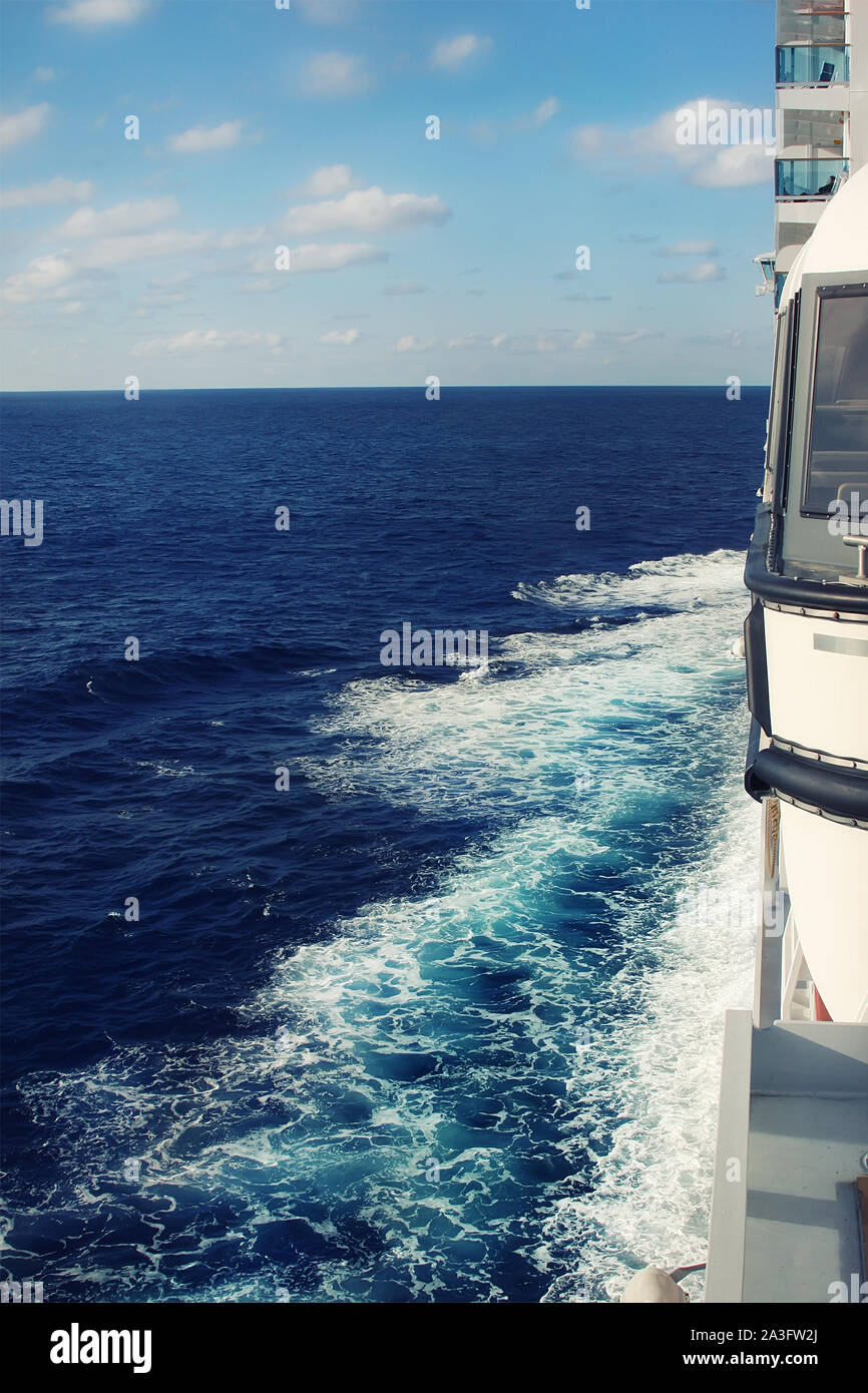 Side view from balcony deck of big cruise ship sailing ocean or sea and ...