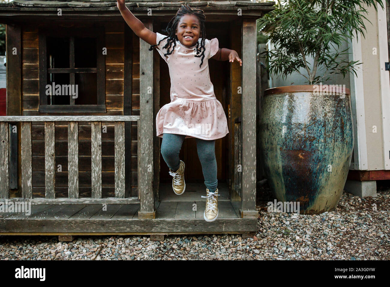 Laughing young black girl with long braids jumping from cabin porch ...