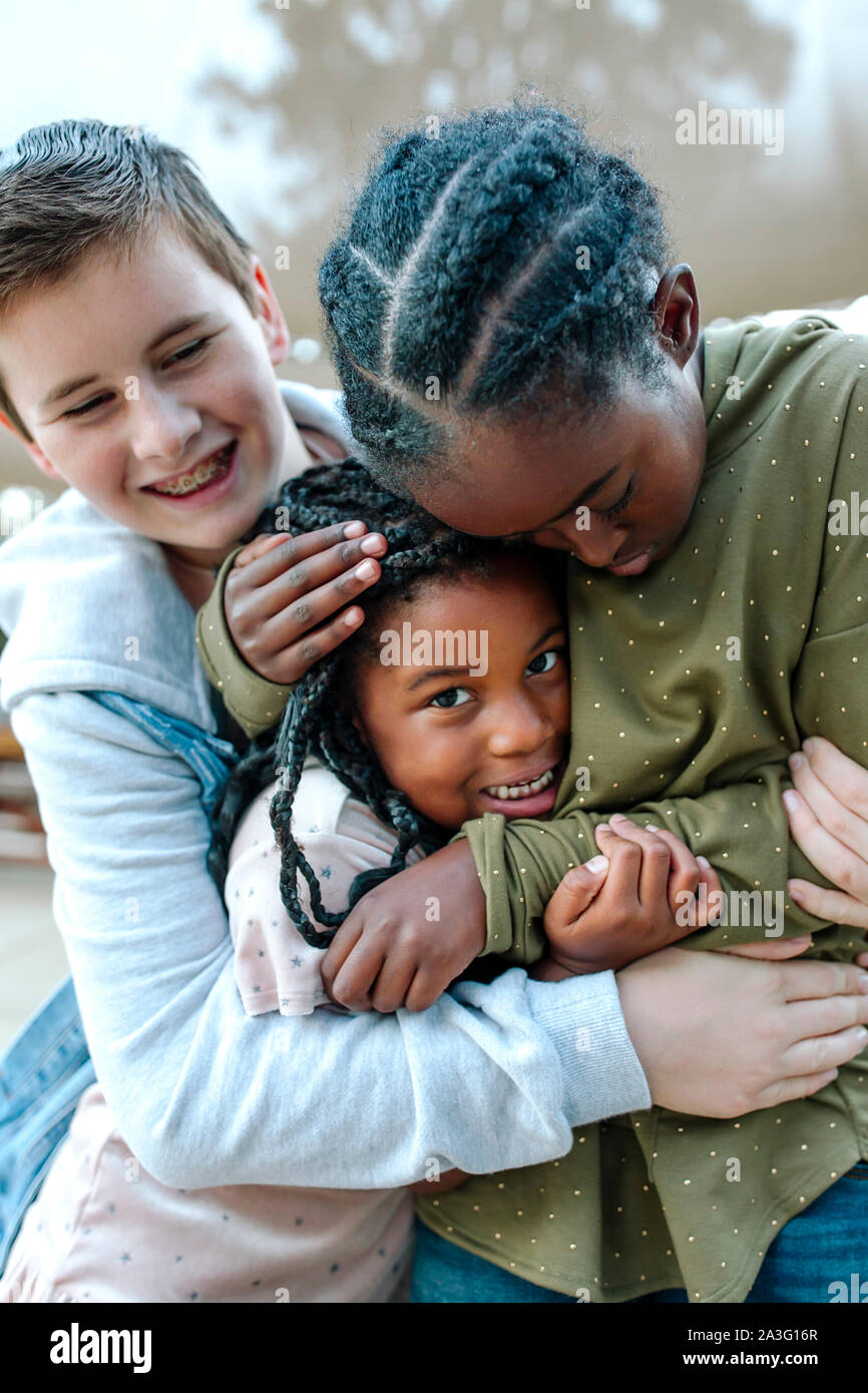 Smiling multiracial siblings hugging young girl with long braids Stock ...