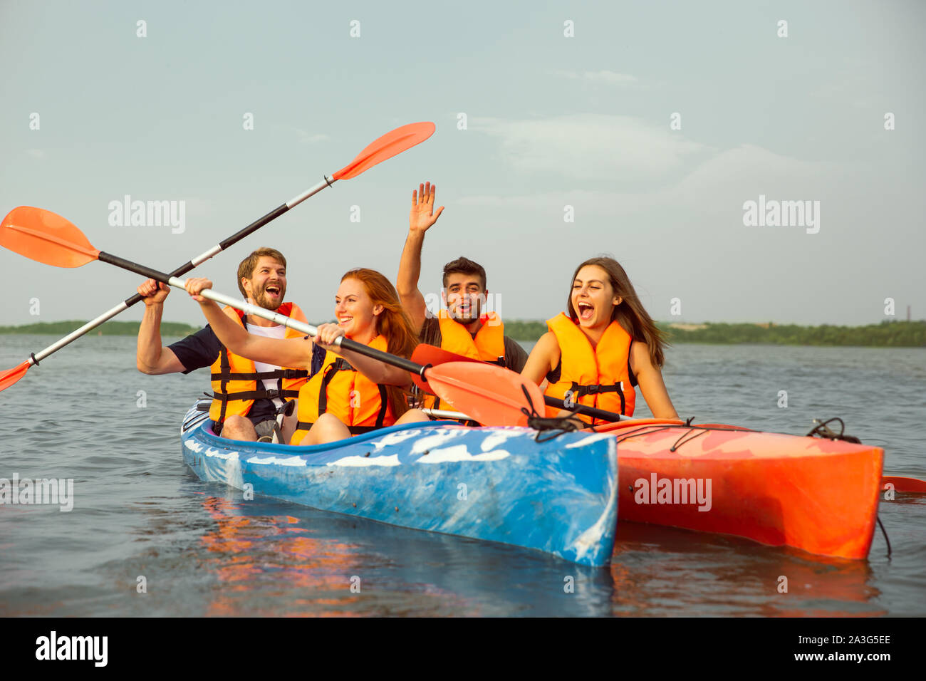 Happy young caucasian group of friends kayaking on river with sunset in ...