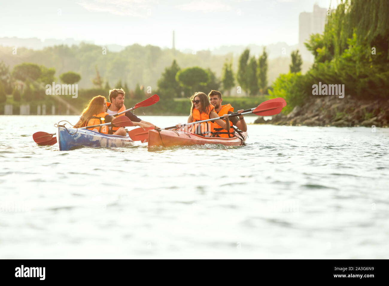 Happy young caucasian group of friends kayaking on river with sunset in ...