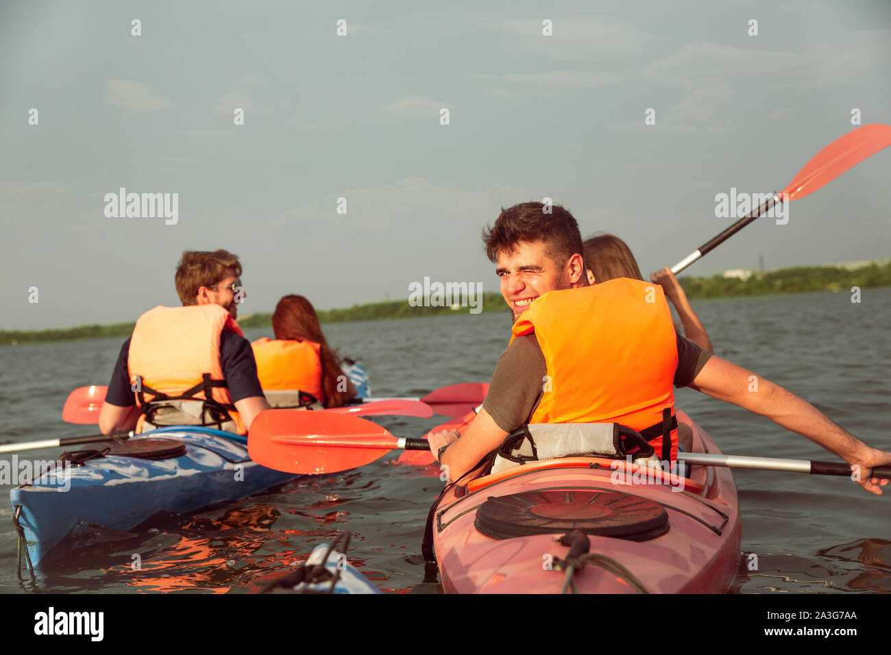 Happy young caucasian group of friends kayaking on river with sunset in ...
