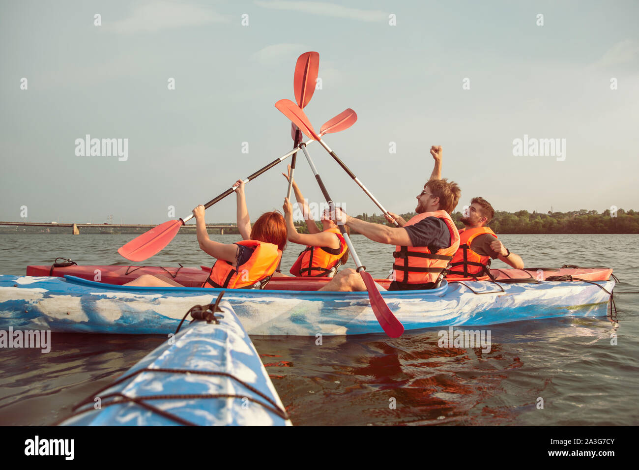 Happy young caucasian group of friends kayaking on river with sunset in ...