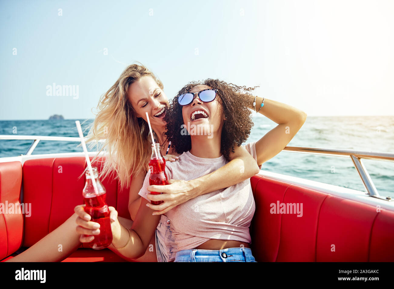 Two young female friends laughing and having drinks while sitting ...