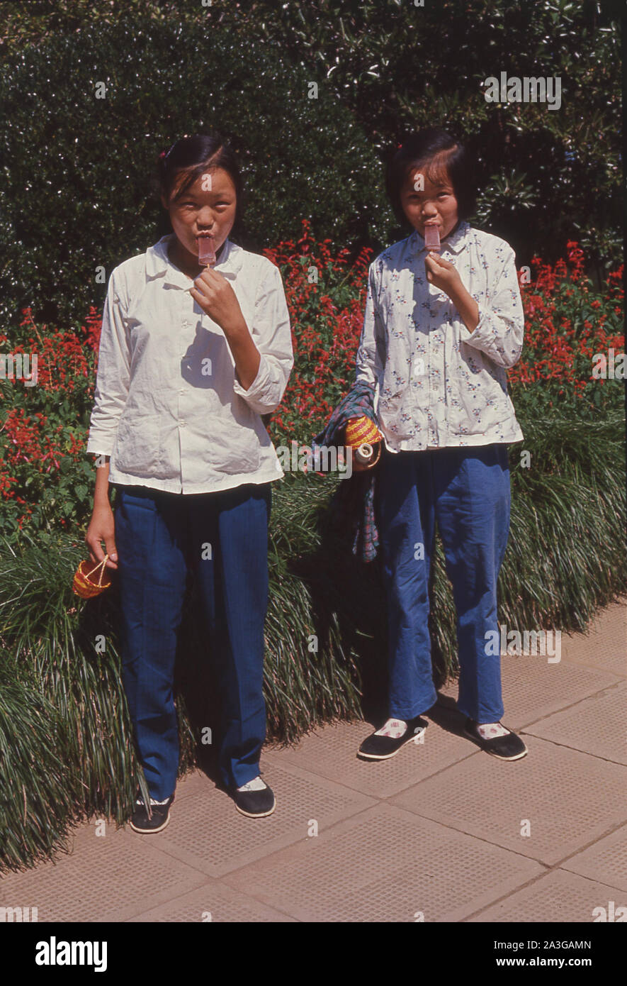 1960s, historical, two young chinese girls standing outside eating ice ...