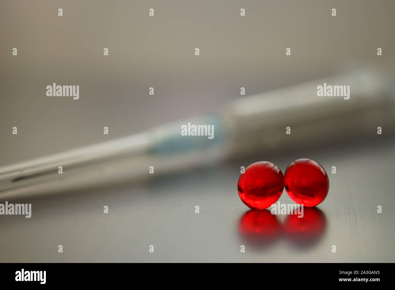 Two red pills and a syringe on a chrome table closeup Stock Photo - Alamy