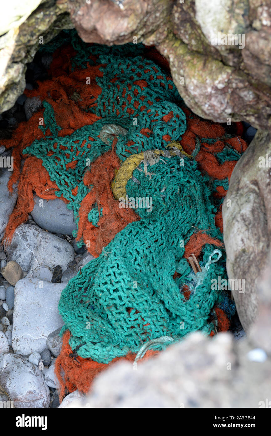 Green and orange fishing net washed up between rocks on Gower Stock ...