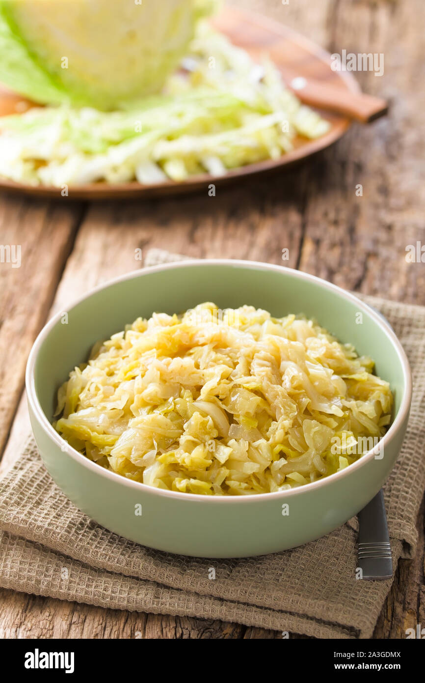 Fresh homemade braised white cabbage in bowl, raw cabbage in the back ...