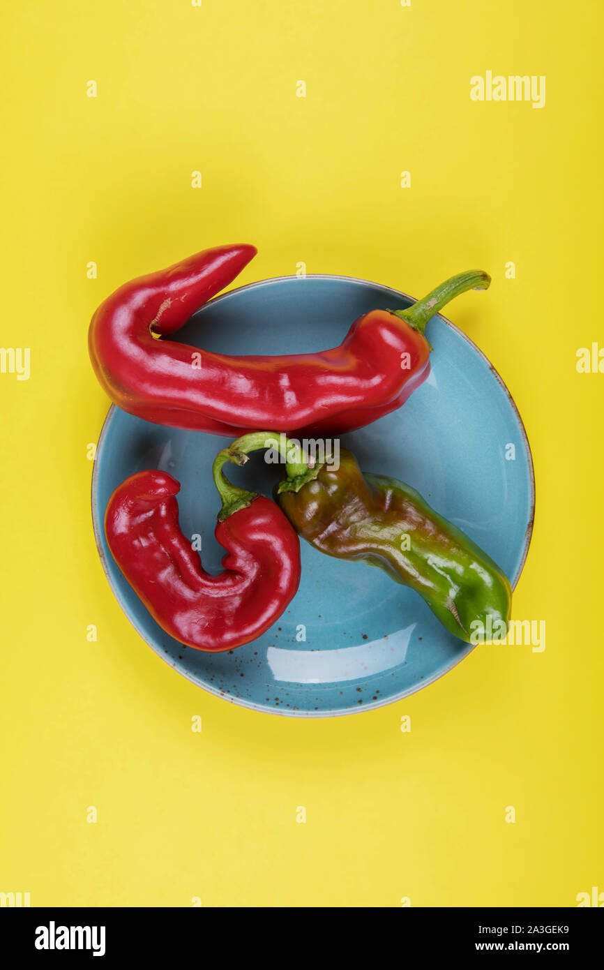 Trendy ugly red chili peppers on a blue plate on a yellow background ...