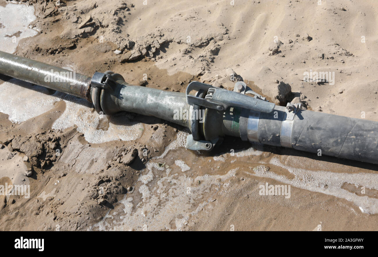 iron pipe for irrigation with a water leak and waste on the arid ground ...