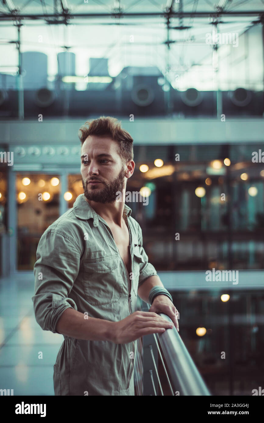 Young handsome man standing at the railing looking unsure or uneasy ...