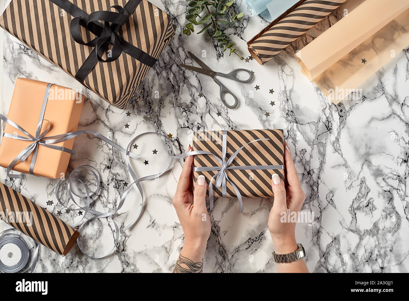 Hands of a woman are holding brown striped paper gift box tied with silver ribbon and bow ...