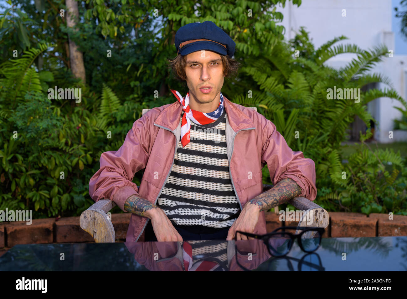 Young handsome rebellious man sitting outdoors and looking at camera ...