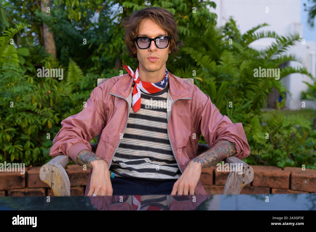 Young handsome rebellious man sitting outdoors and looking at camera ...