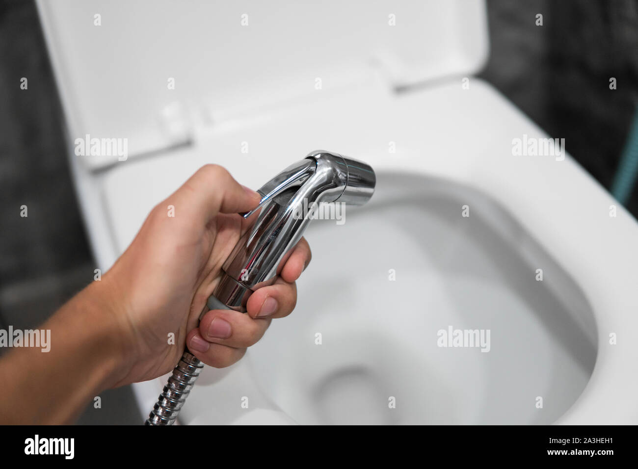 Using of bidet shower with a white toilet. Bidet shower in male hand ...