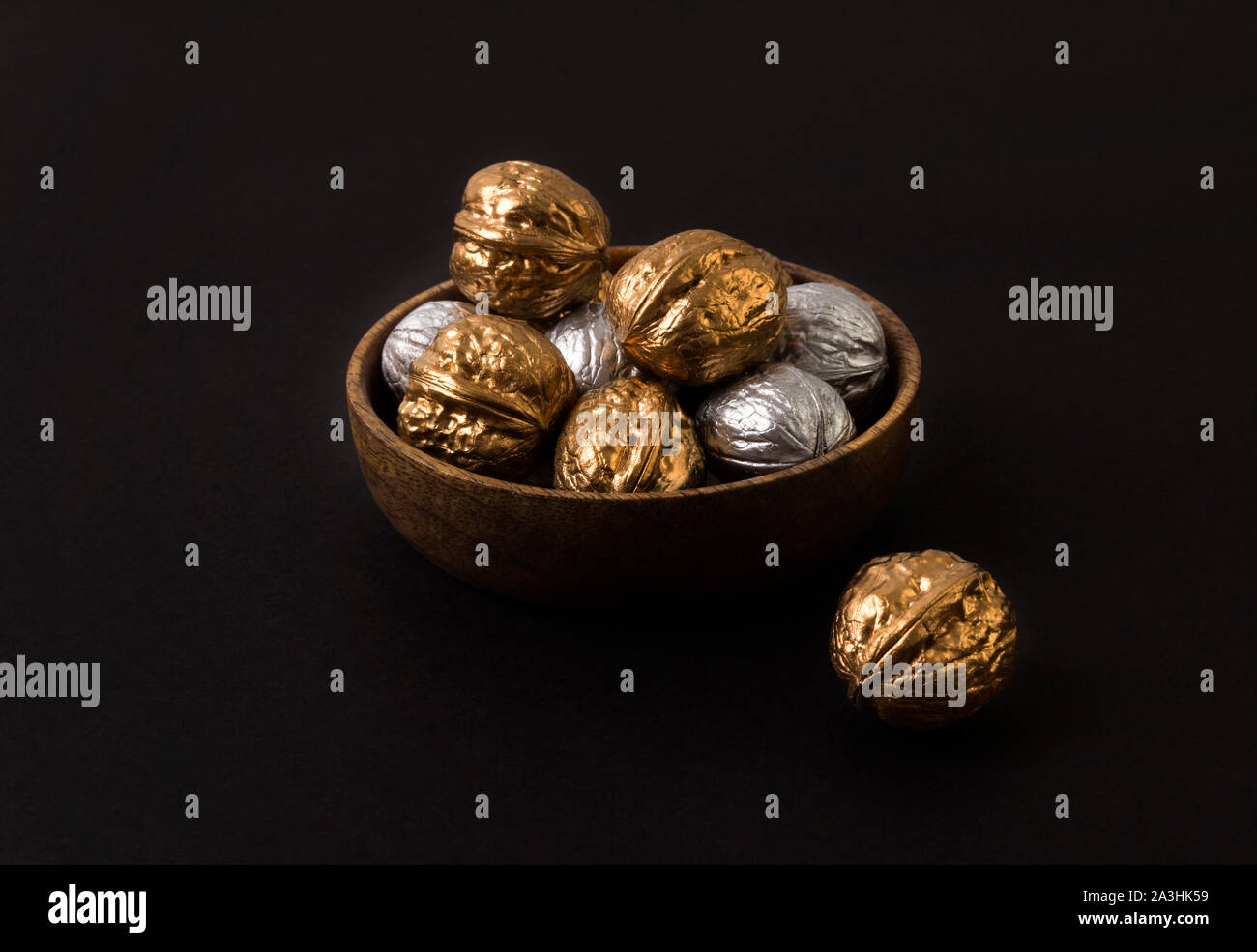 Painted golden and silver walnuts on wooden plate on black background ...