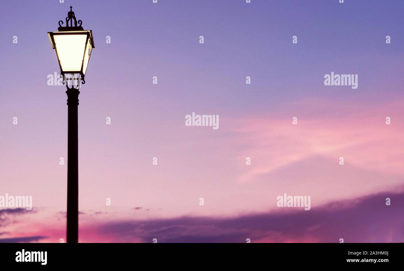 Streetlight isolated in a pink sky at sunset. Lamppost lit with a ...