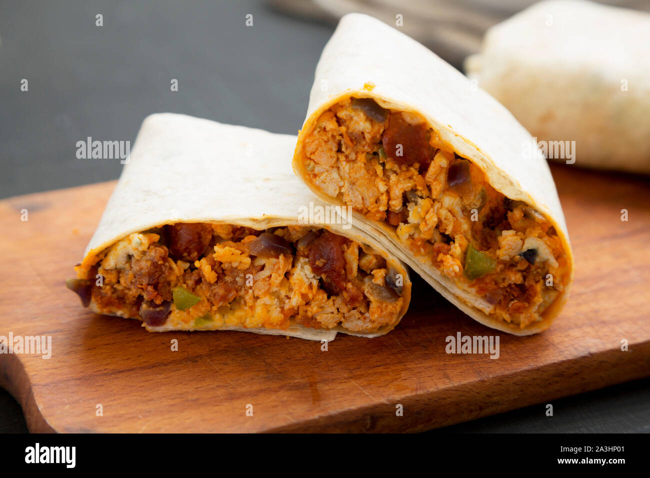 Homemade chorizo breakfast burritos on a rustic wooden board on a black ...