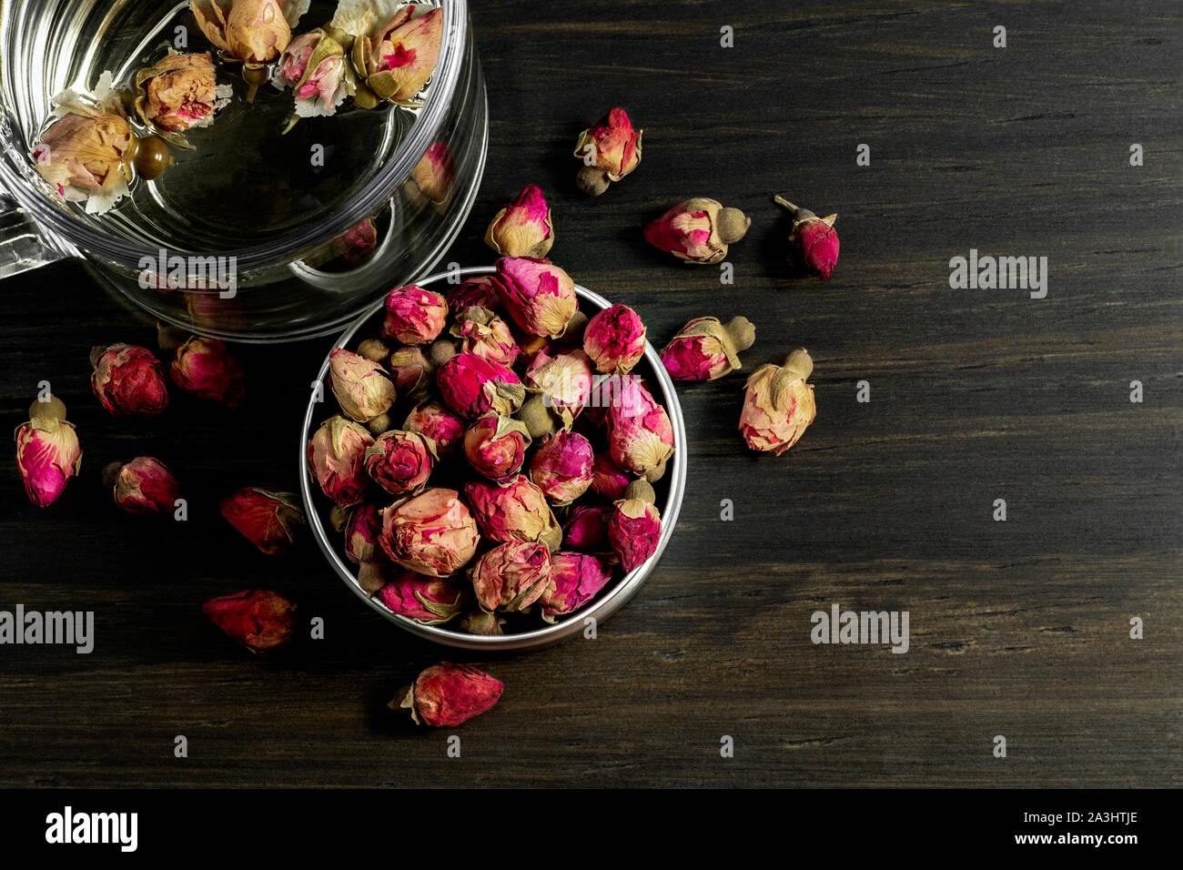 dried rose buds tea in metal container accompanied by glass mug on wood ...