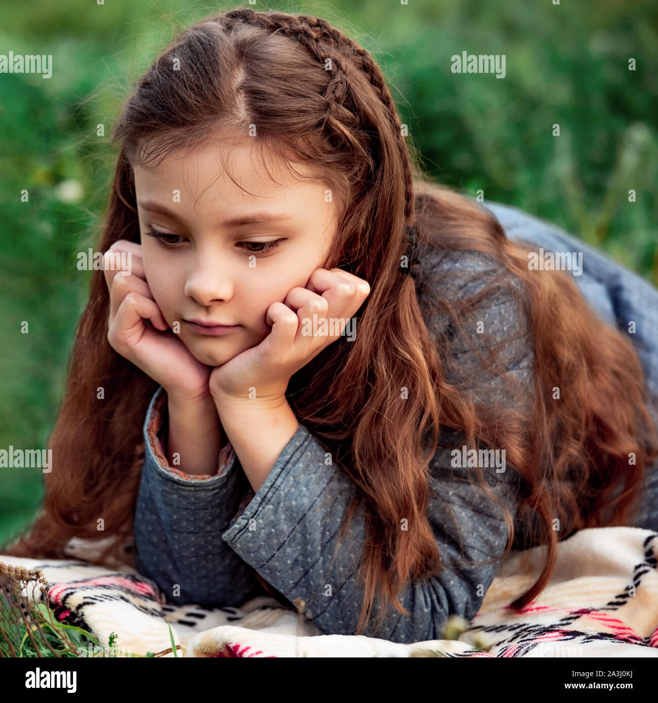 Unhappy kid girl with beautiful hair looking down with sad eyes. Hands ...