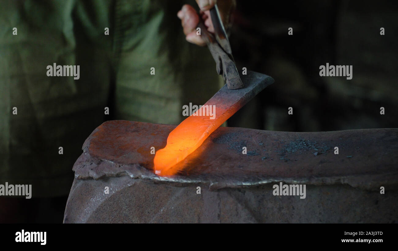 The blacksmith holds in the ticks red-hot metal on the anvil. Anvil in ...