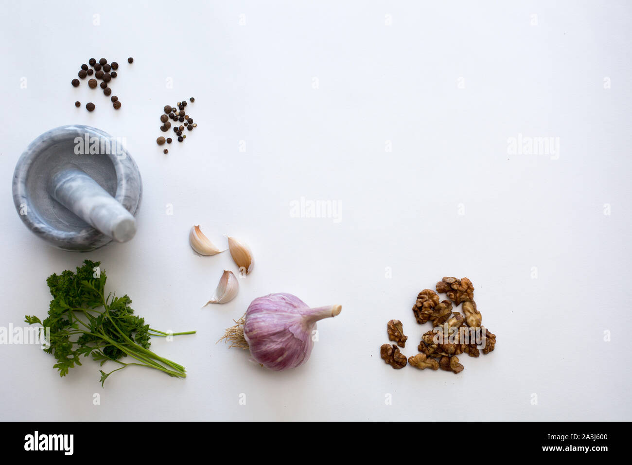 Mortar and pestle, garlic, spices, greenary and nuts on a white ...