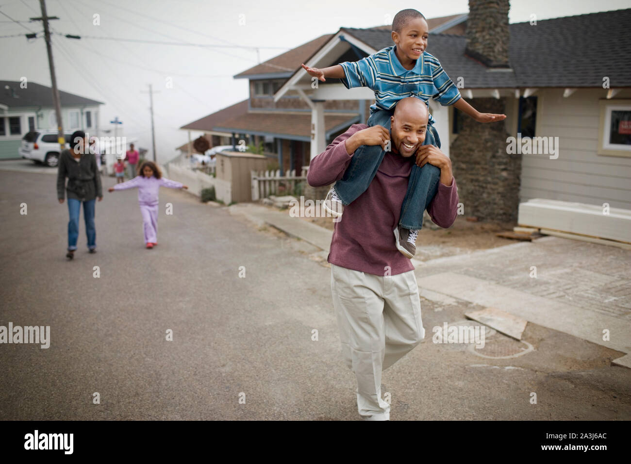 Father carrying his young son on his shoulders down a suburban street ...