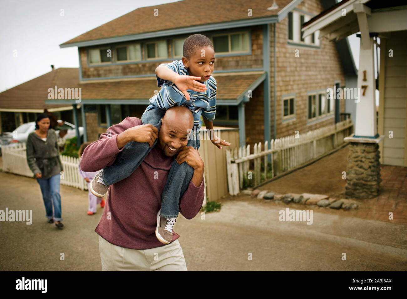 Father carrying his young son on his shoulders down a suburban street ...