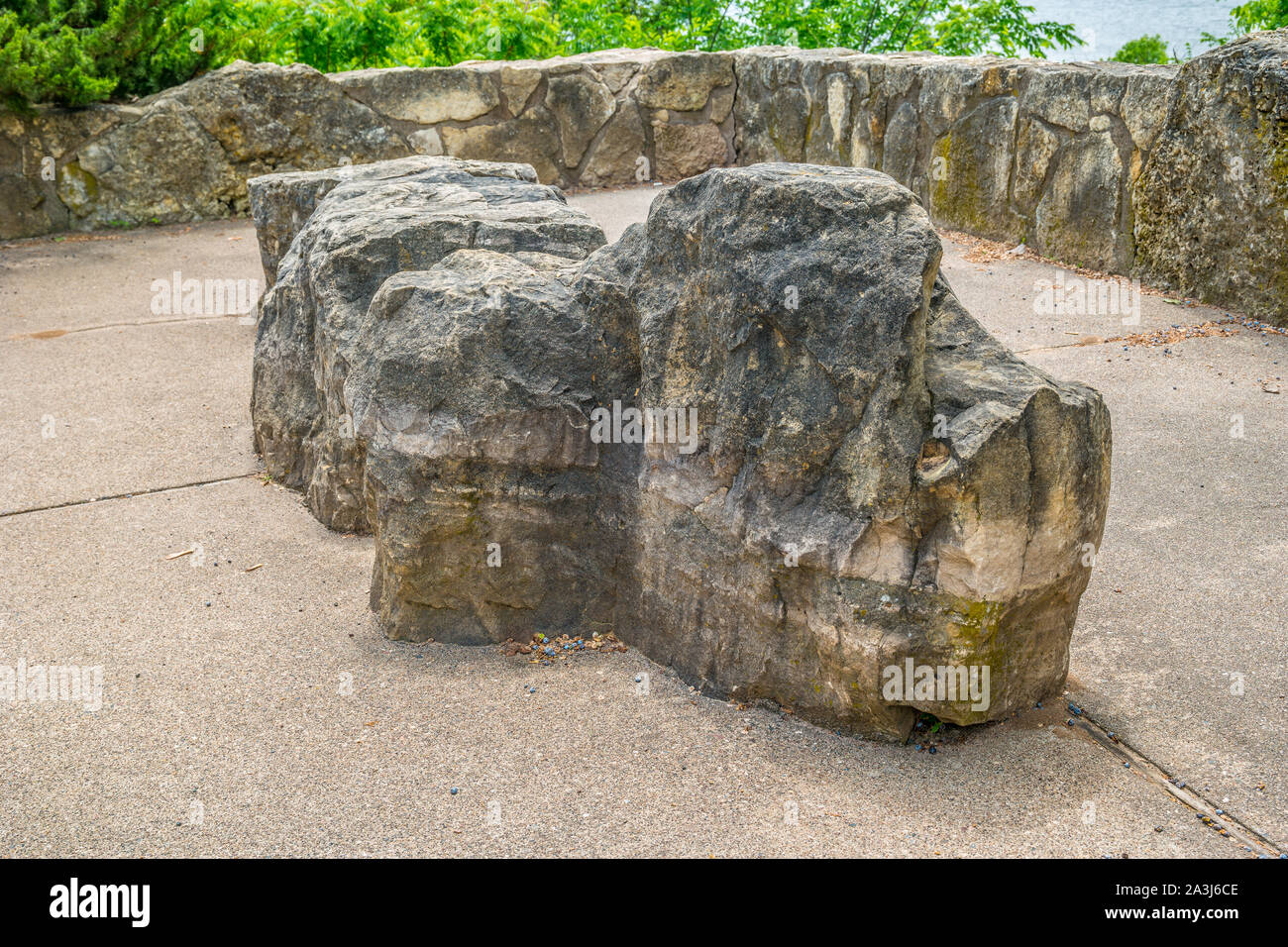 A large rock bench closeup at a roadside overlook park with trees and a ...
