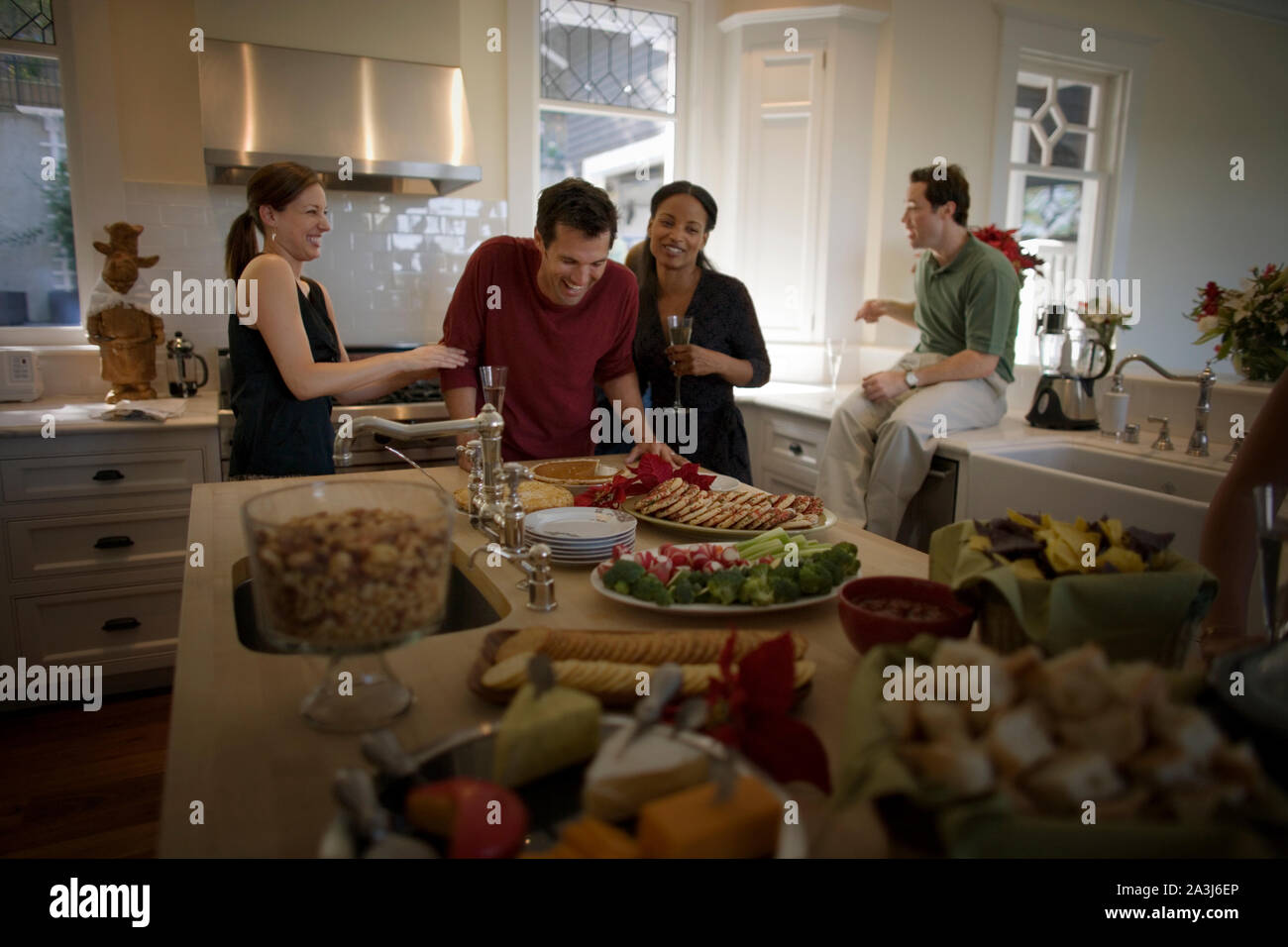 Group of friends standing around party food laid out on a kitchen bench ...