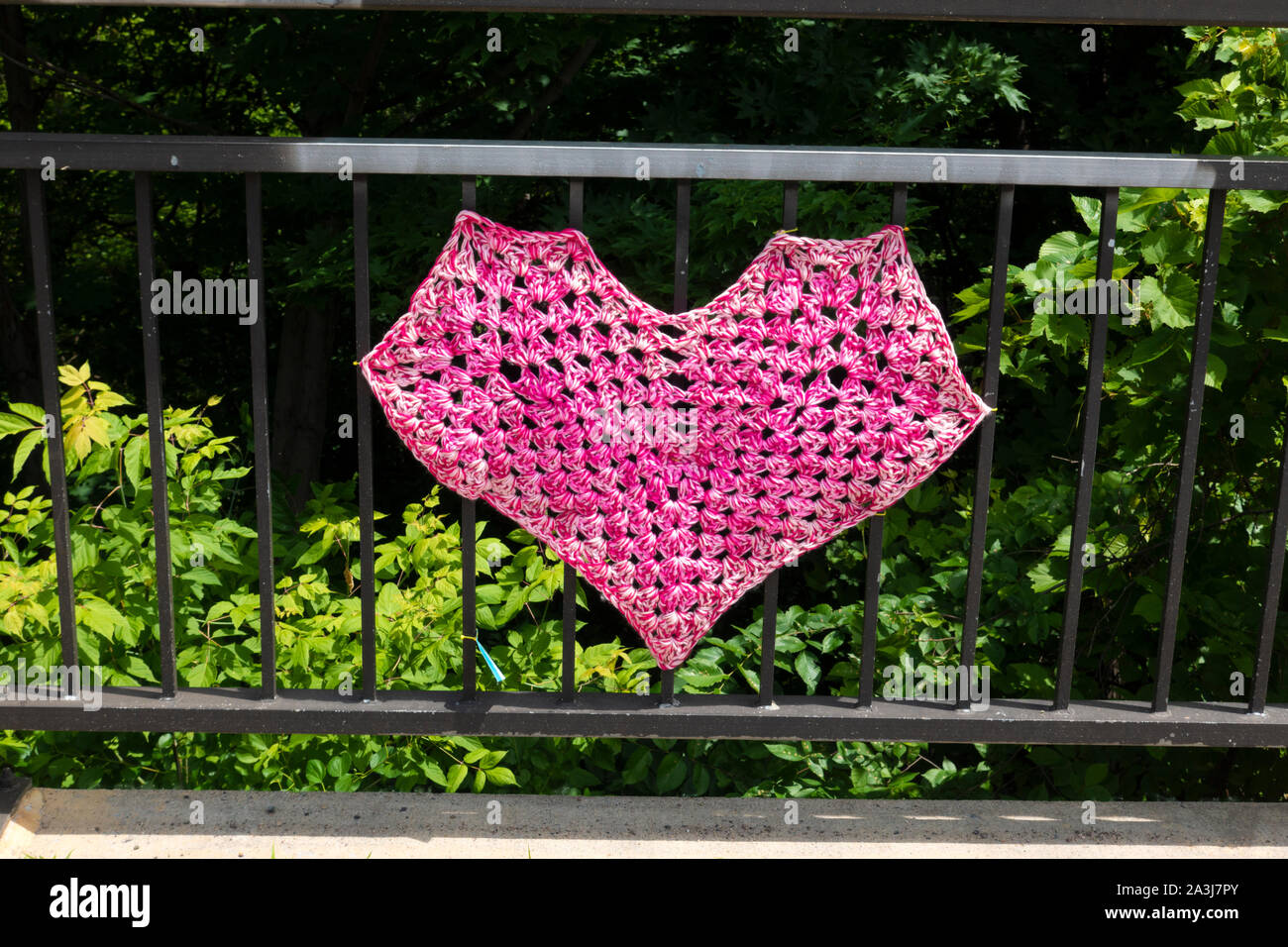 Creative large pink crocheted heart fastened to an outdoor fence. St ...