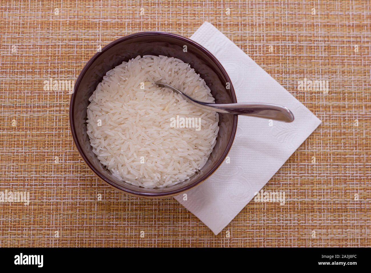 Raw white rice in cup and silver spoon on napkin on gunny background on ...