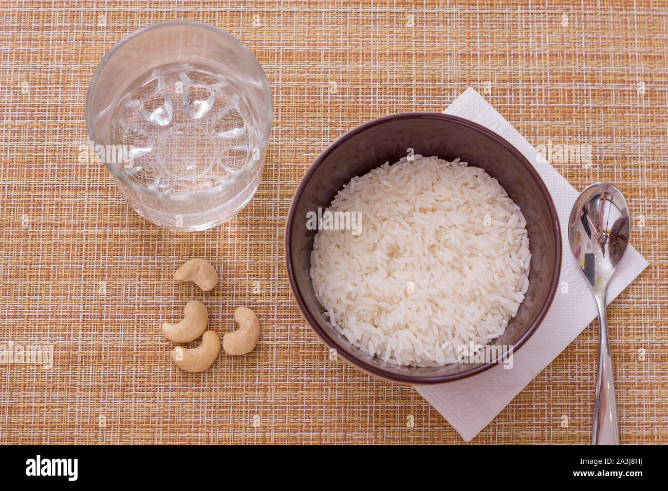 Raw white rice in cup, cup of water, cashew nuts and silver spoon on ...