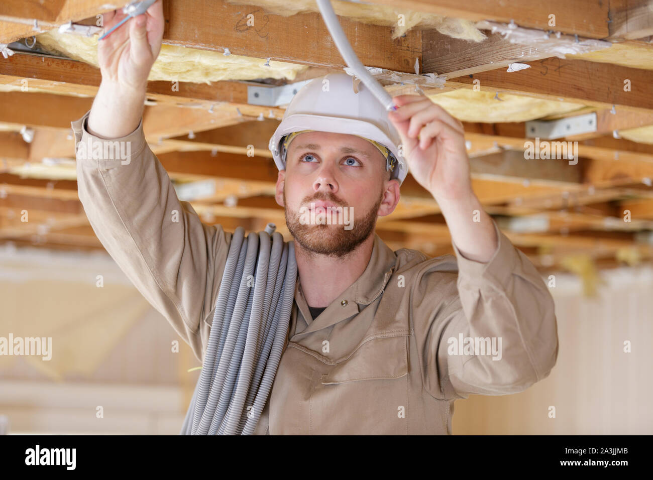 male builder in a helmet fixing cables Stock Photo - Alamy