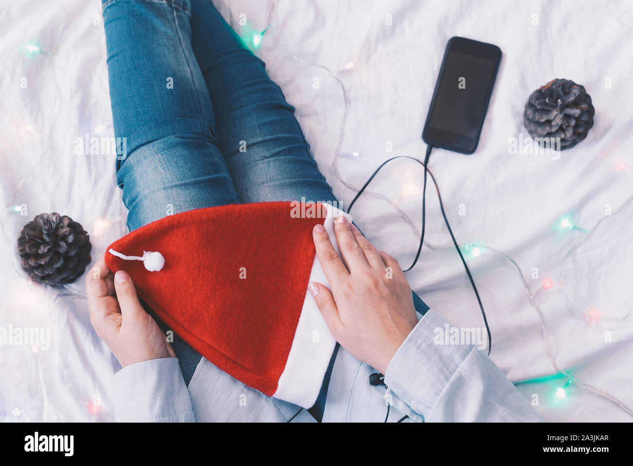 Female listening to music in bed. Pine tree cones, Santa Claus cap and ...