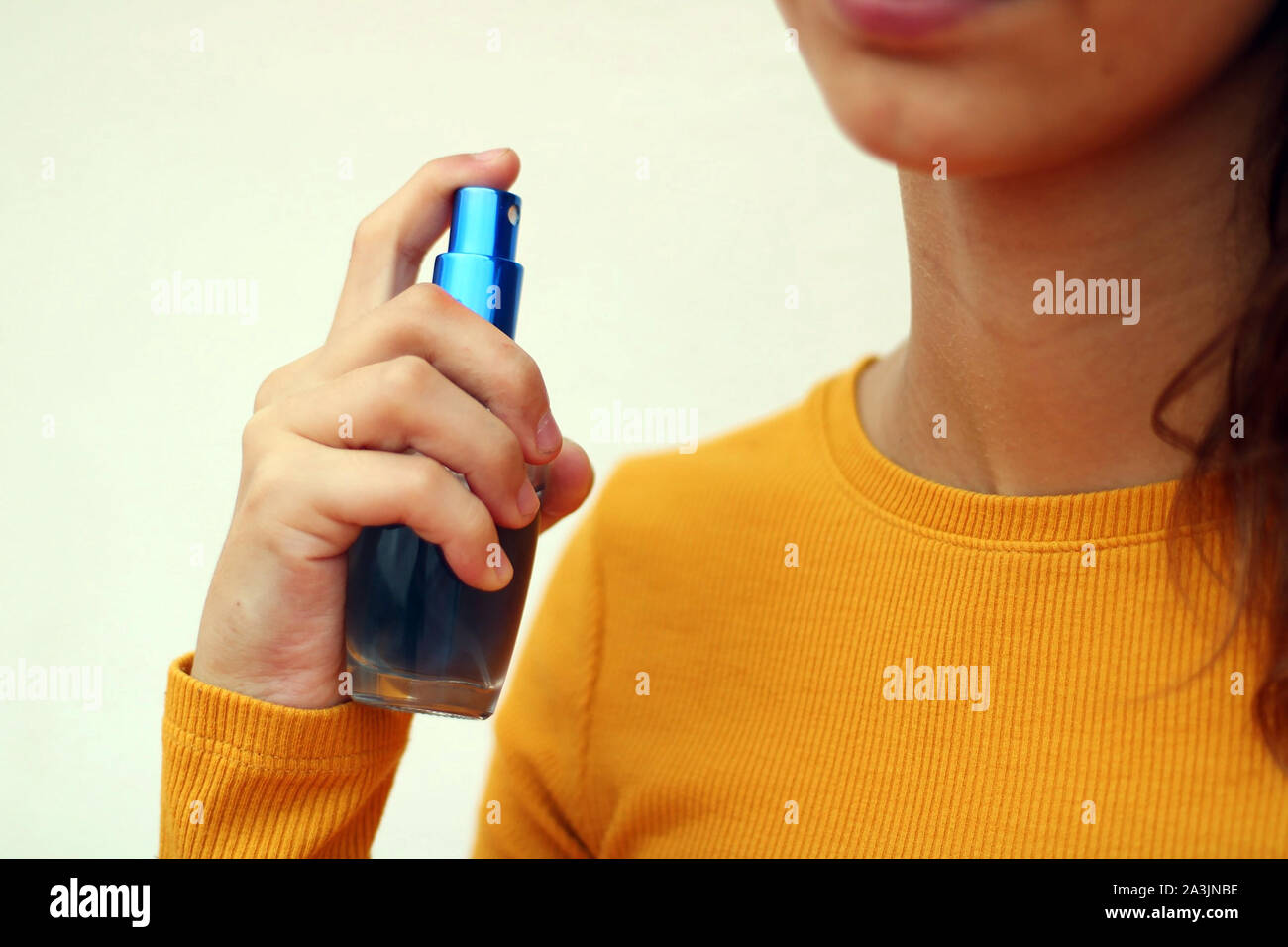 Beautiful young girl dressed in yellow, spraying perfume from a blue ...