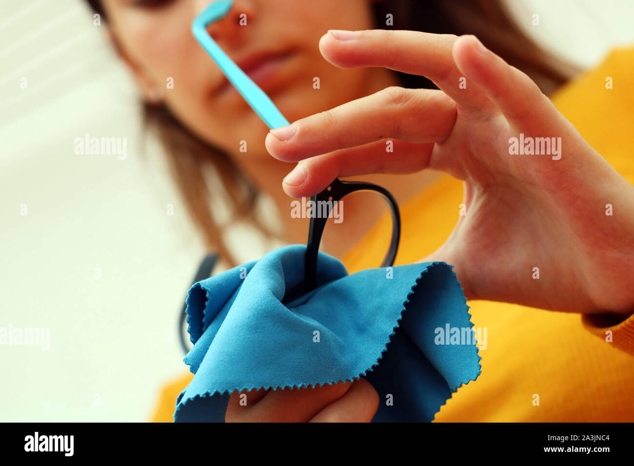 Pretty young girl cleaning her blue glasses with a blue rag. Blue ...