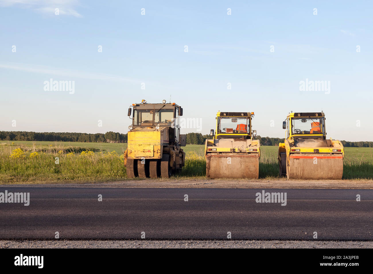 Three large yellow asphalt paving rollers standing on the side of the ...