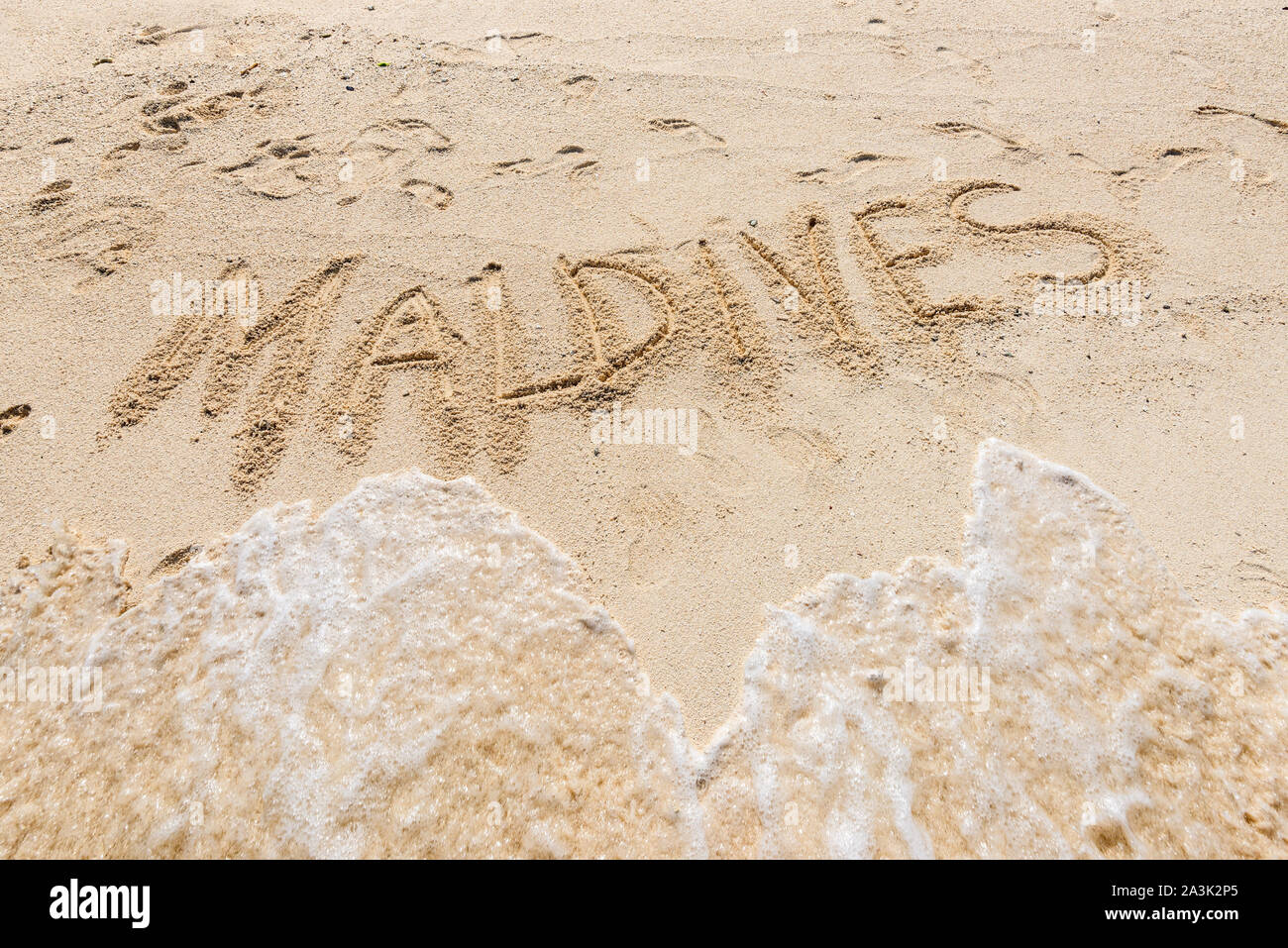Handwriting word "Maldives" on maldivian beach drawn on sand and sea ...
