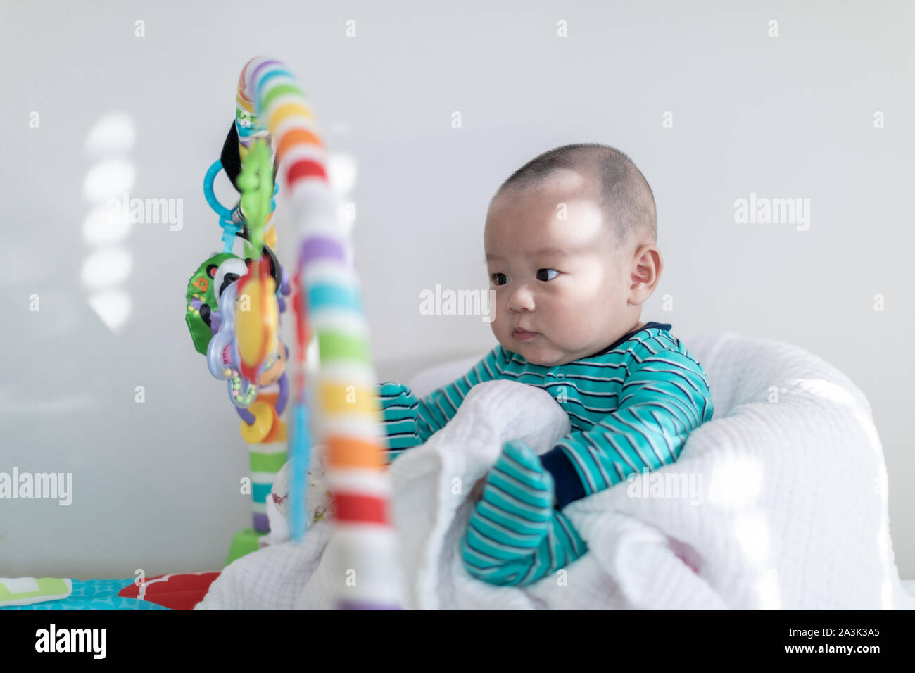Cute baby sitting on a chair in front of colorful rainbow toys in the ...